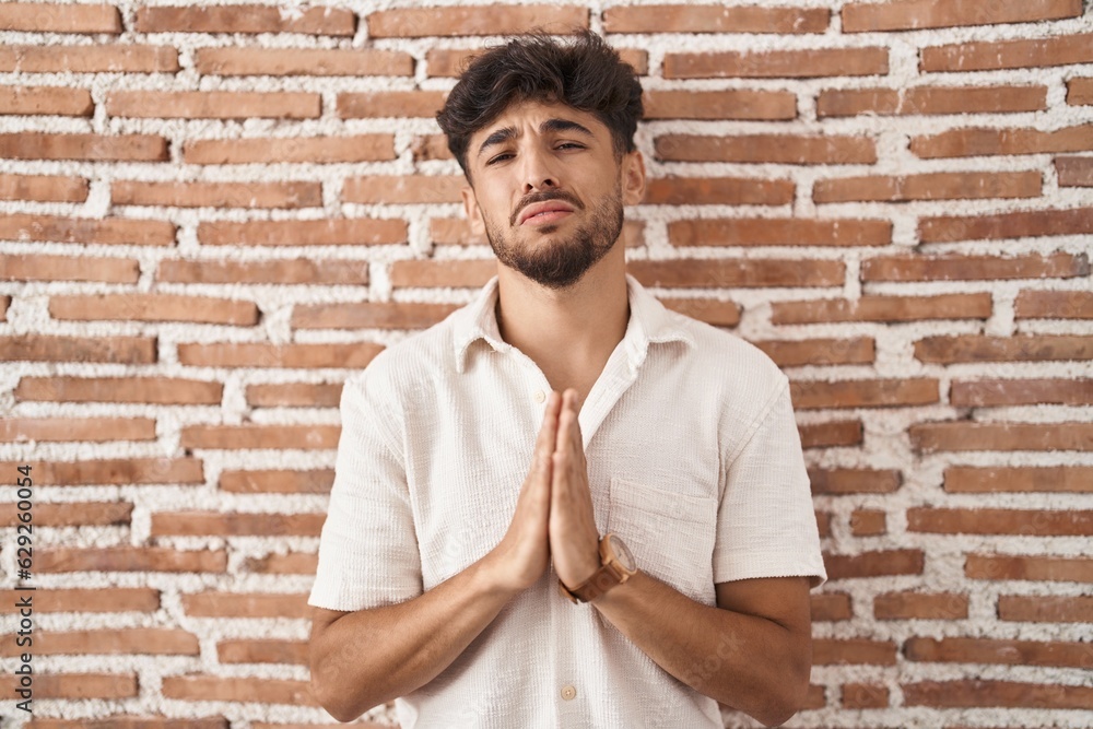 Arab man with beard standing over bricks wall background begging and ...