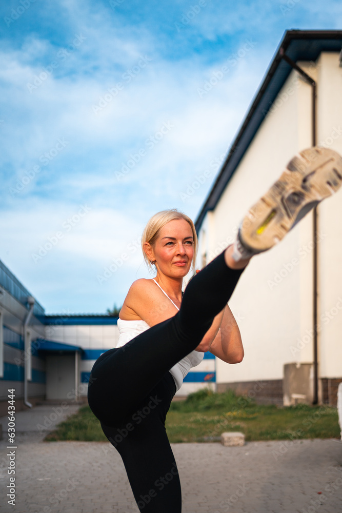 Adult beautiful blonde woman doing box kicks exercises workout outdoors ...