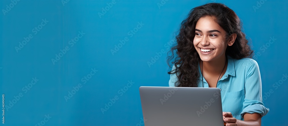Smiling Indian teen girl using laptop for online study on blue ...