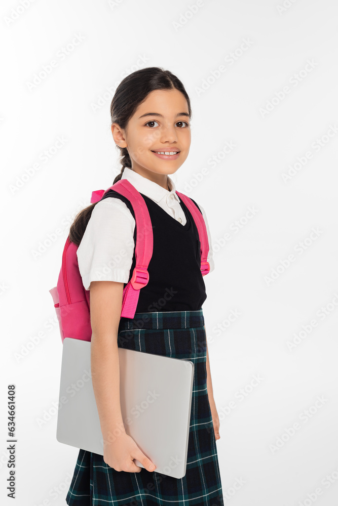 positive schoolgirl holding laptop and looking at camera, girl in ...