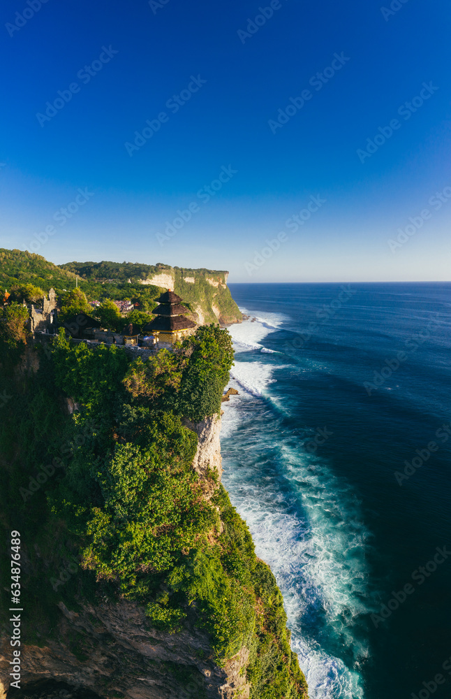 At the foot of imposing cliffs, waves surge with fervent energy, their ...