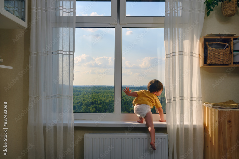 The little baby is dangerously climbing up the window sill, oblivious ...