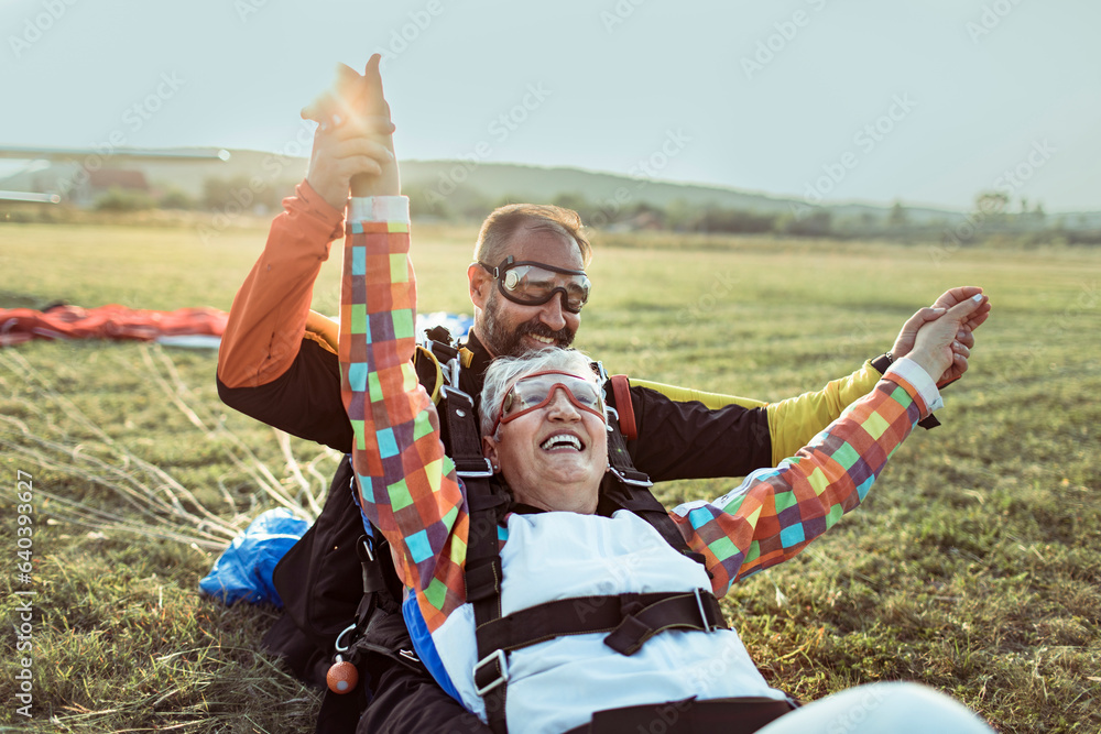 Senior woman skydiving with her instructor and landing on a field with ...