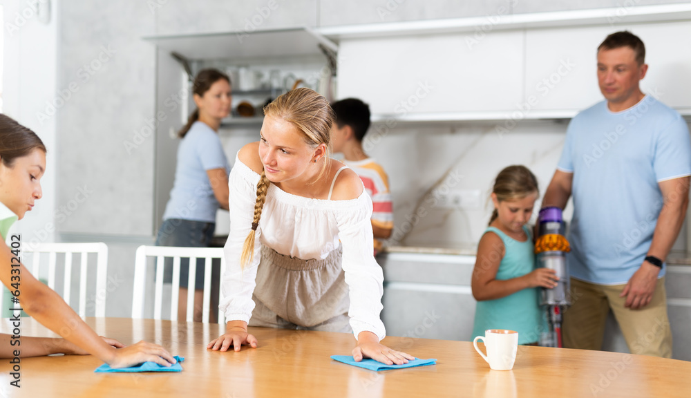 ภาพถ่าย Stock Two teenage girls wipe table and help their mother clean ...