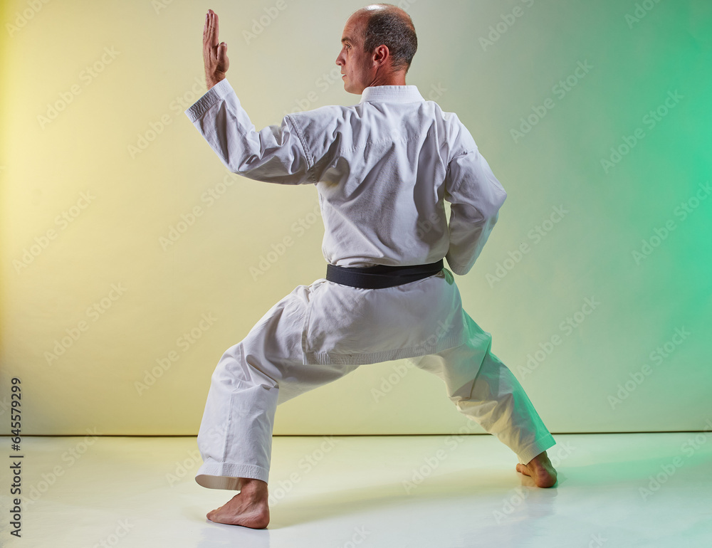 Adult athlete with black belt doing formal exercises against color ...