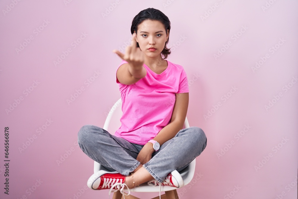 Hispanic young woman sitting on chair over pink background showing ...