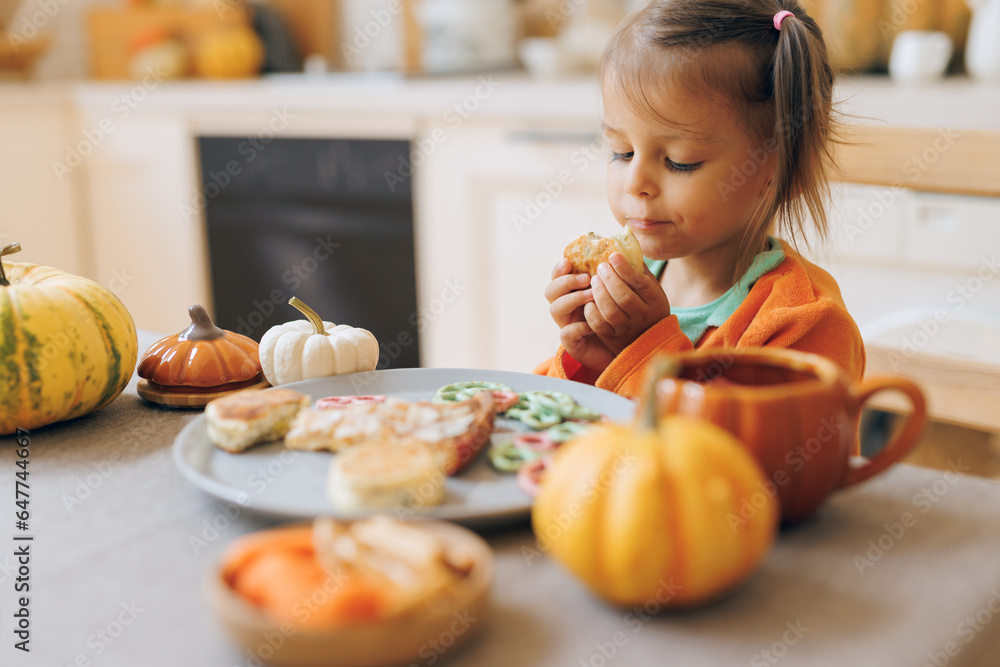 Happy Halloween! Little cute girl eating cookies in the kitchen ...