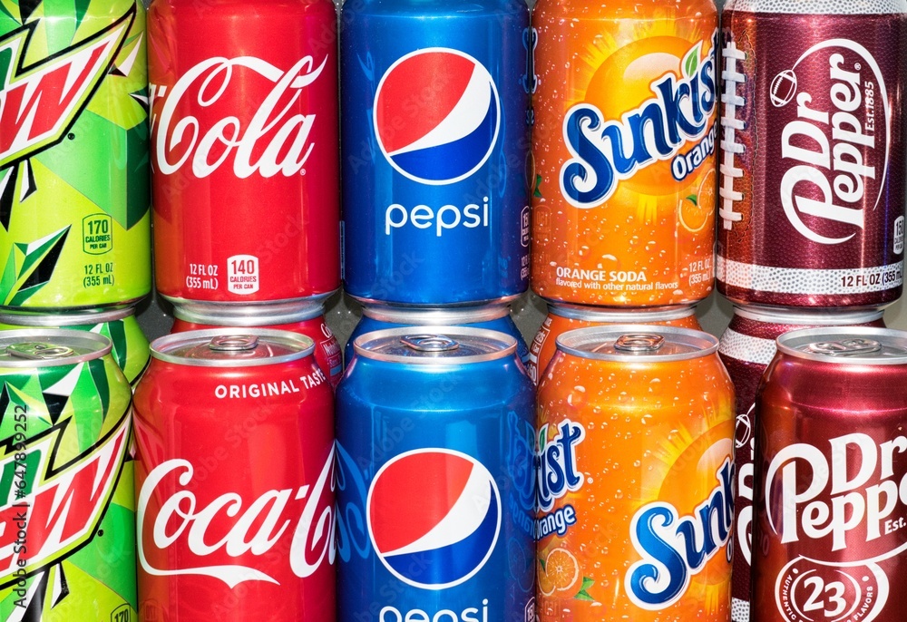 Assorted unopened carbonated soda cans in various flavors stacked ...