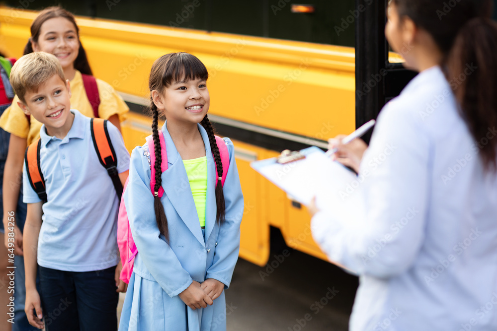 Black female teacher updating check list of children entering school ...