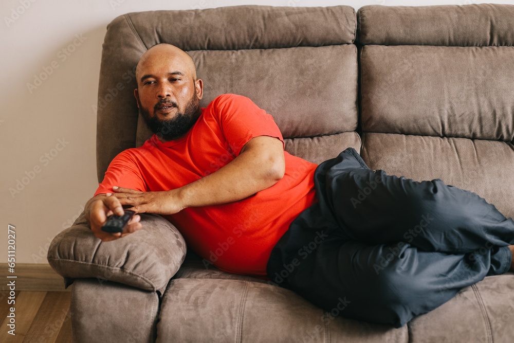 Fat and bald man watching TV while lying on sofa at home. Stock Photo ...