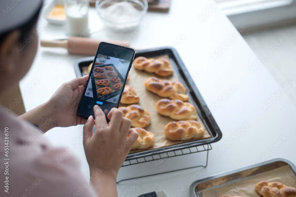 Female bakery chef or baker uses a with her smartphone mobile to take ...