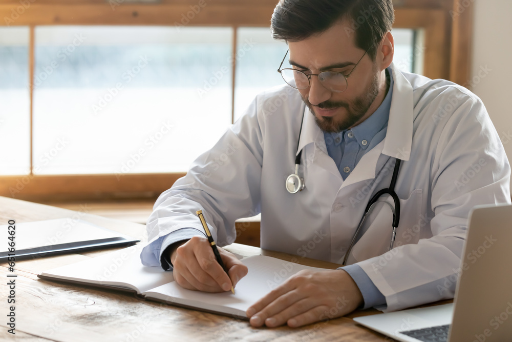Focused doctor wearing glasses writing illness history, sitting at ...