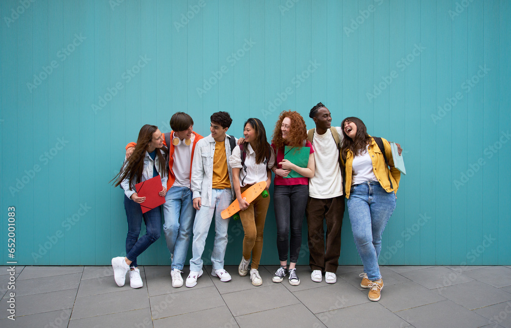 Large group of cheerful young people leaning against blue wall ...