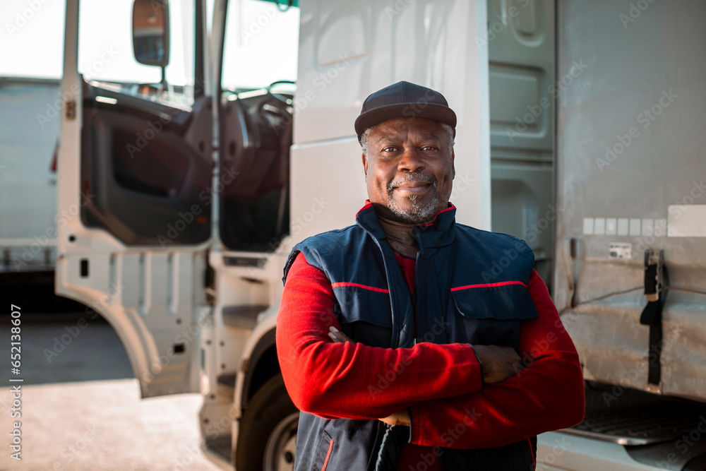 Middle aged male african truck driver standing by his truck and working ...