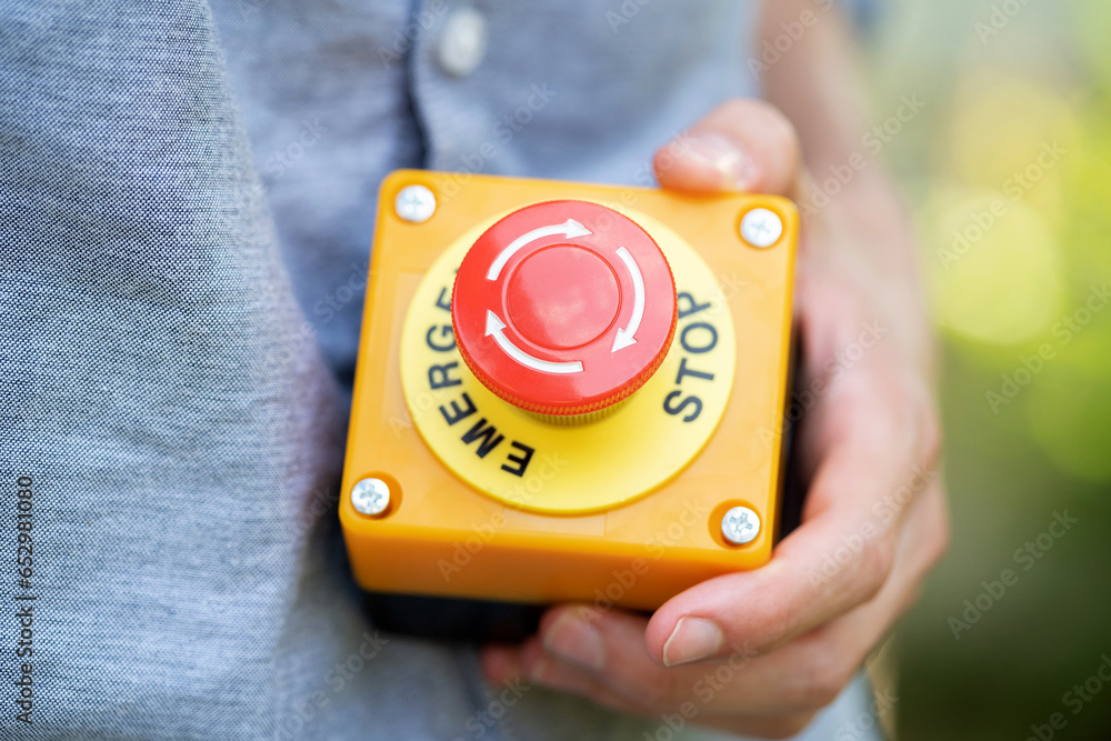 Man holding a large red industrial machinery emergency stop button in ...
