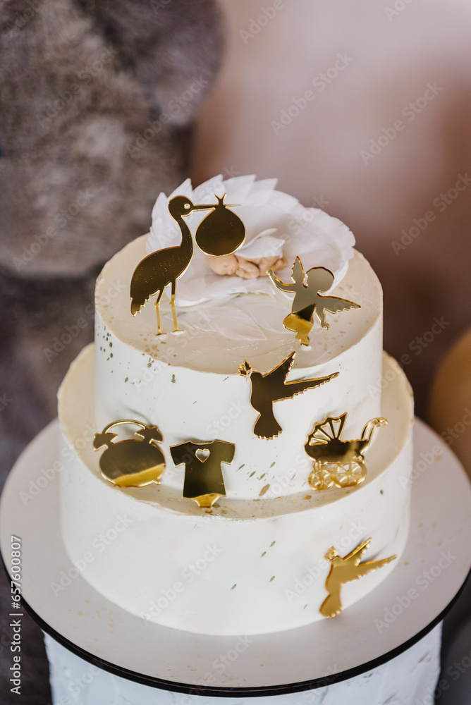 Cake with a figure angel, stork carrying a baby, and golden decor. Celebration baptism concept ...