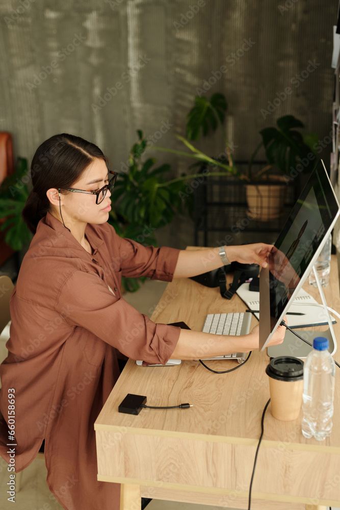 Side view of young female photographer adjusting computer monitor while ...