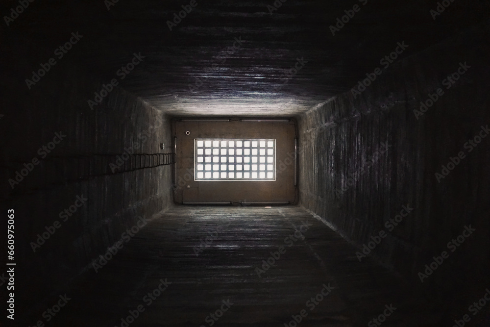 Light behind barred window in the dark prison cell - empty jail interior with grey concrete ...