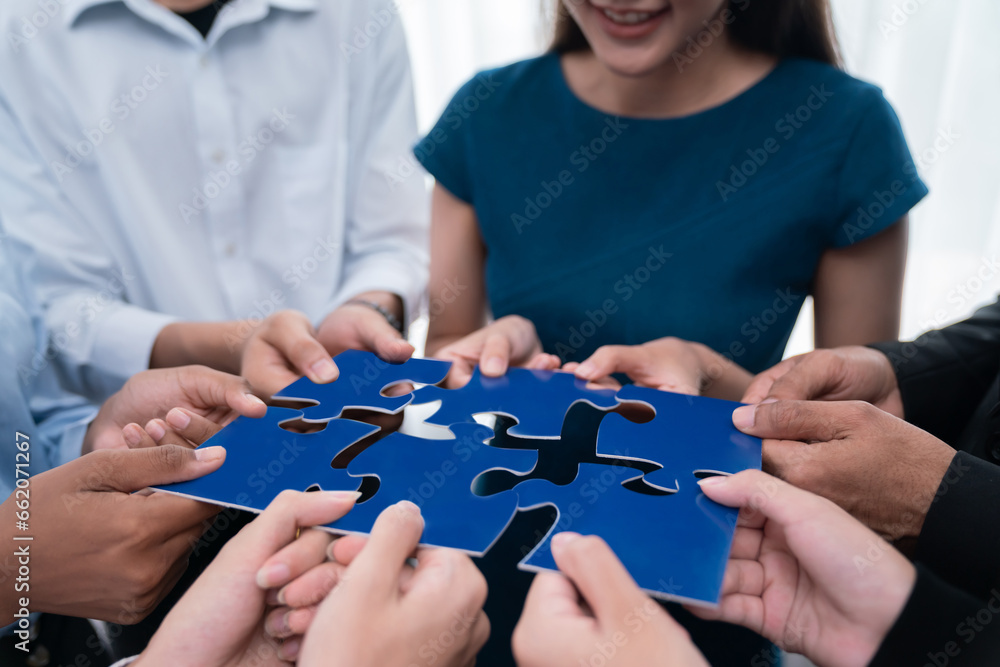 Diverse corporate officer workers collaborate in office, connecting puzzle pieces to represent ...