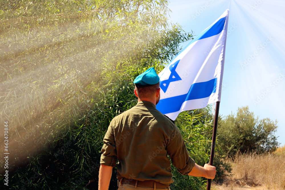 Foto Israeli soldier stands in a field with Flag of Israel in the ...