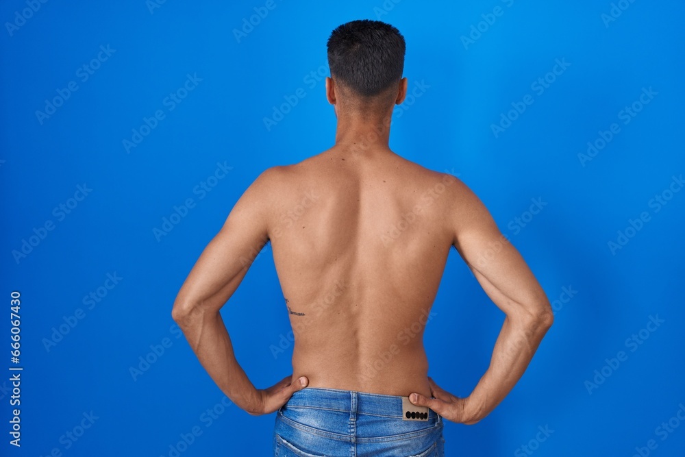 Young hispanic man standing shirtless over blue background standing ...