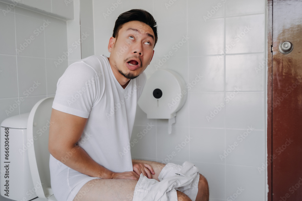 Funny face asian man pushing poop in the toilet as he has constipation. Stock Photo | Adobe Stock