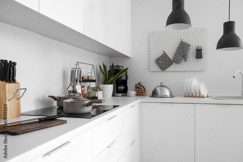 White kitchen counters with electric stove, cooking pots and utensils ...