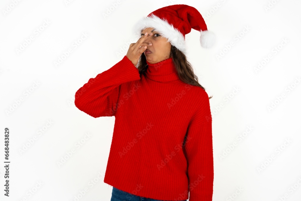Beautiful girl wearing red sweater and Santa hat smelling something ...