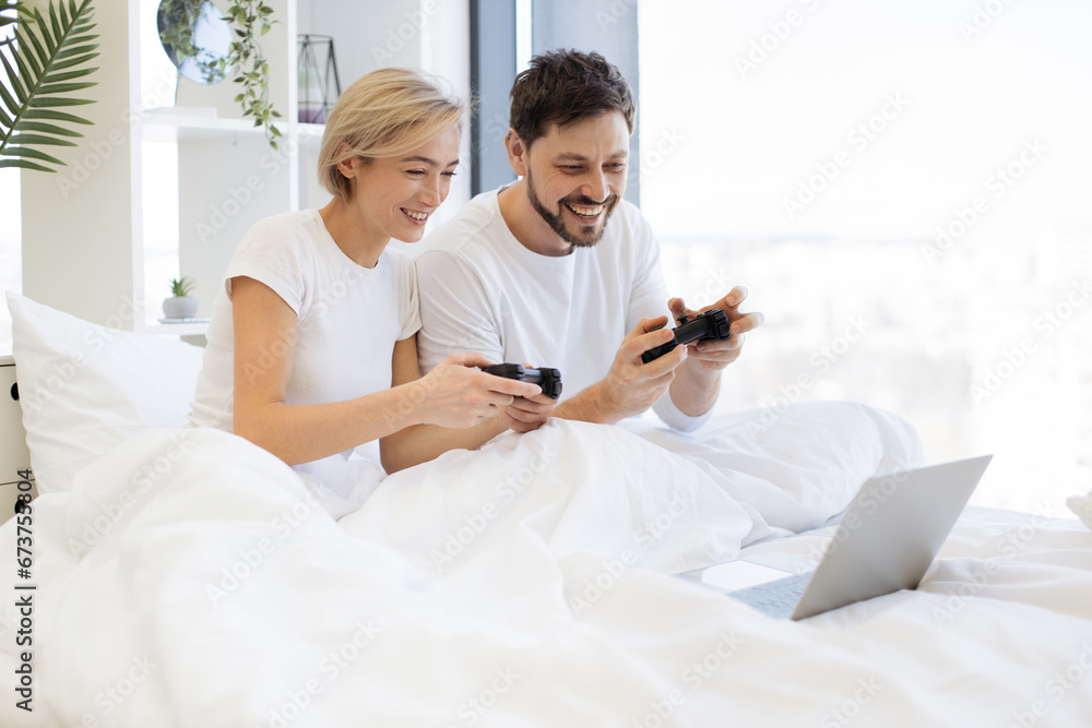 Caucasian couple playing video games while lying under blanket at home ...