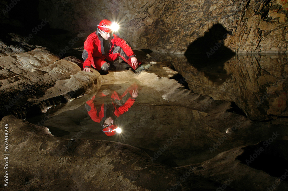 Reflection of a spelunker in a cave water pool. Acetylene gas lamp on ...