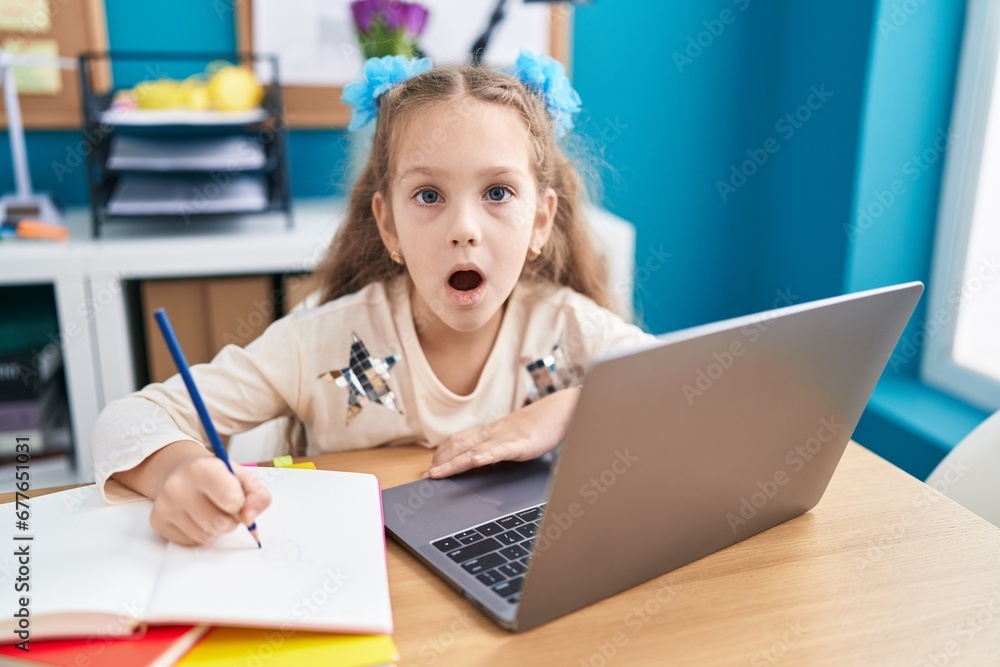 Young little girl sitting on the table doing homework with laptop ...