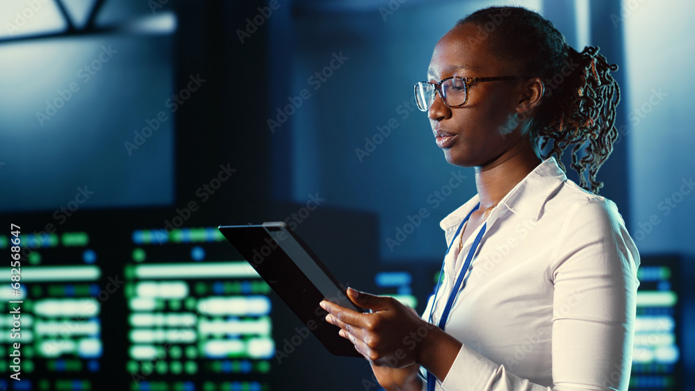 African american woman walking through server farm rows providing processing resources for ...