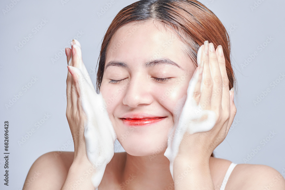 Smiling young woman washing foam face by natural foamy gel. satisfied girl with bare shoulders ...