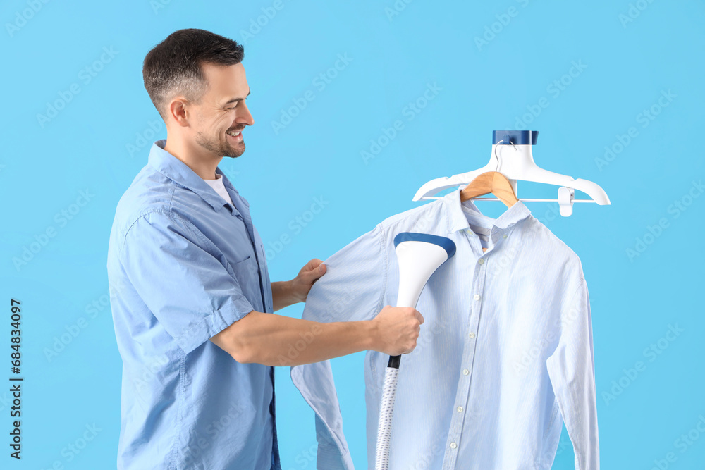 Handsome man steaming shirt with steamer on blue background Stock Photo ...