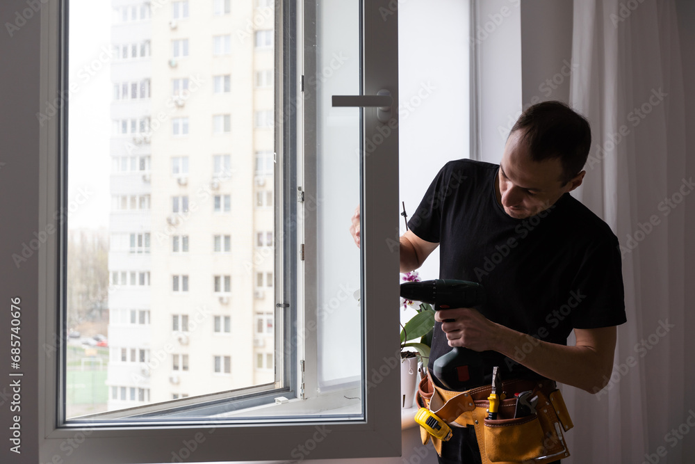 Handyman using a cordless screwdriver to install a window handle ...
