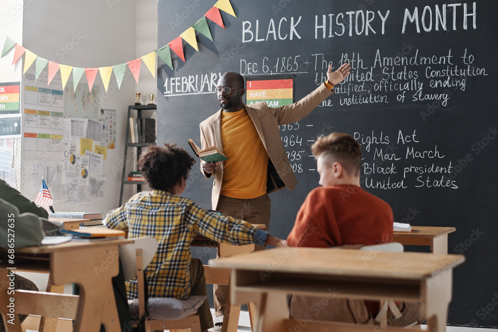 African AMerican teacher pointing at blackboard and talking about Black ...