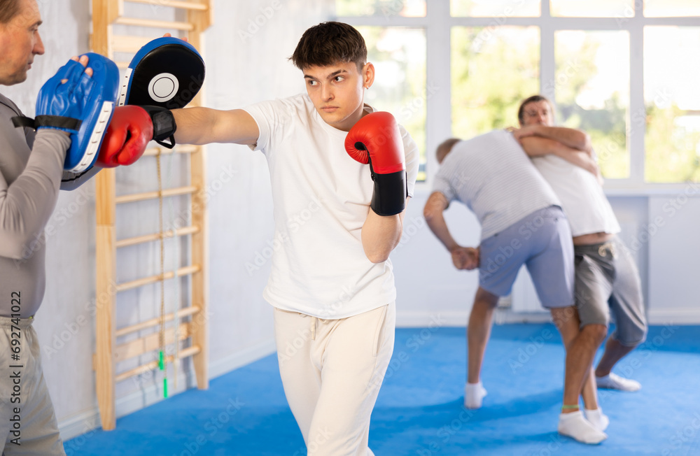 Coach holding mitts during self defence training in gym with young guy ...