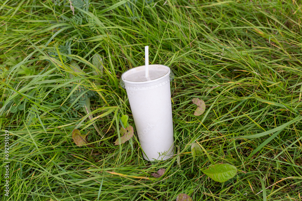 A white paper cup of coffee lies in the grass, polluting nature. The ...