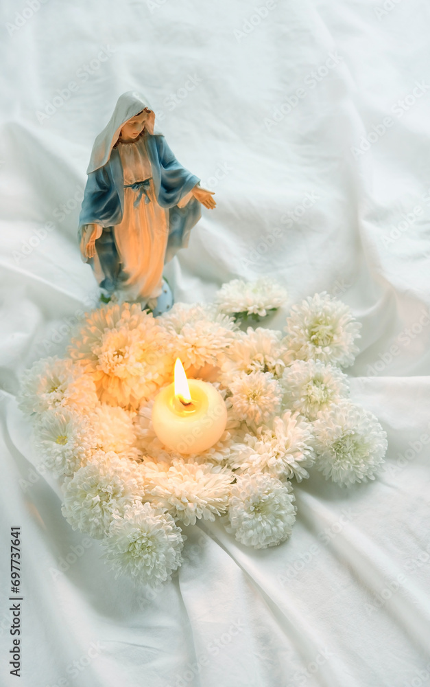 Virgin Mary figurine with white flowers and burning candle on abstract ...