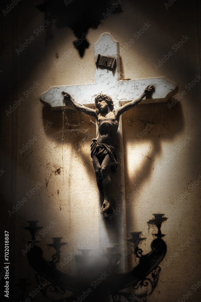 Crucified Jesus Christ figure in a ray of sunlight in a grave with spider webs hanging on him ...