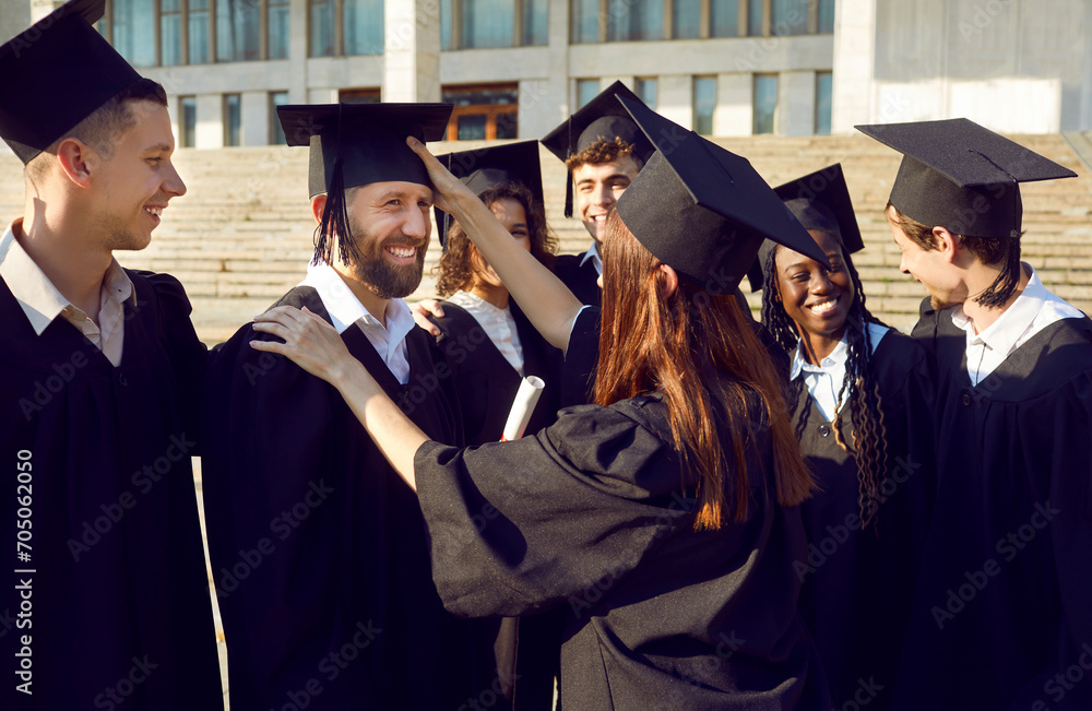 Student girl puts black academic hat on head of happy young man. Group ...