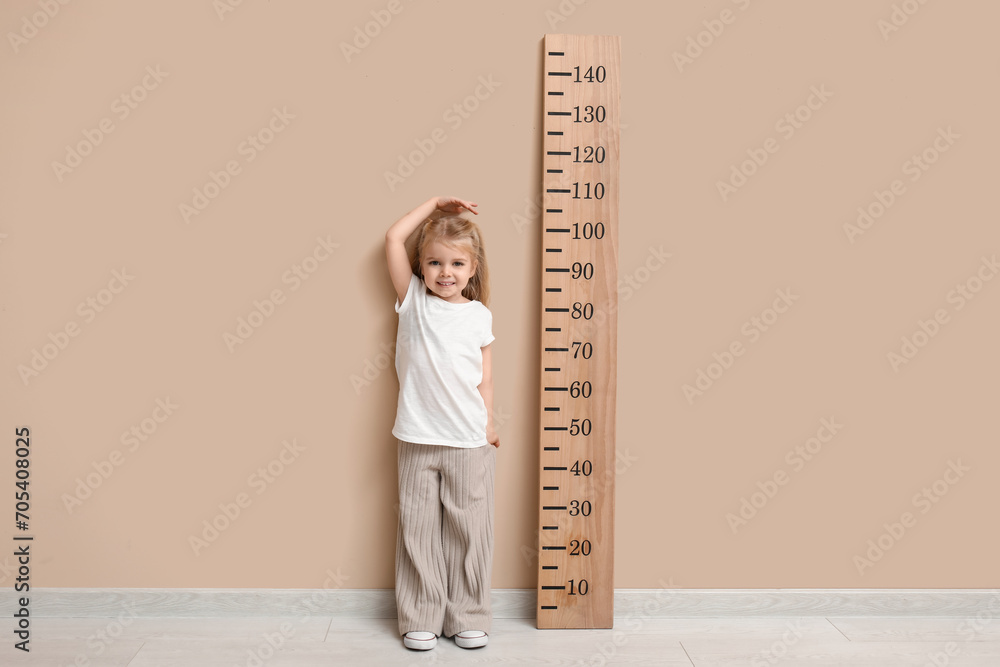 Cute little girl measuring height near beige wall Stock Photo | Adobe Stock