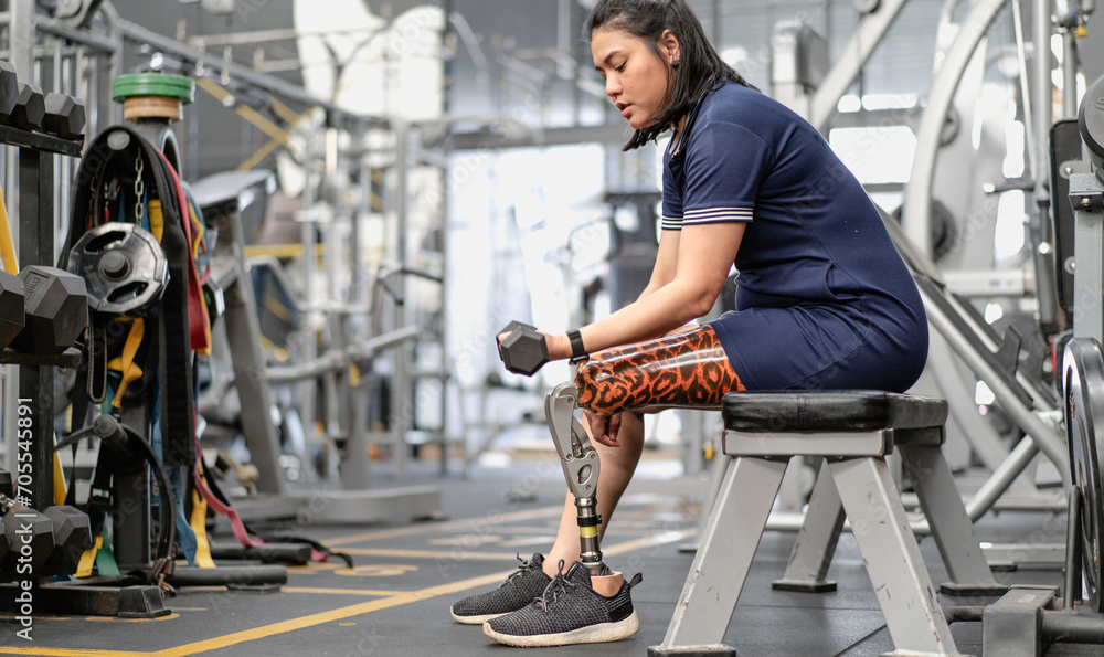 Woman with prosthetic leg sitting in gym lifting dumbbell weight ...