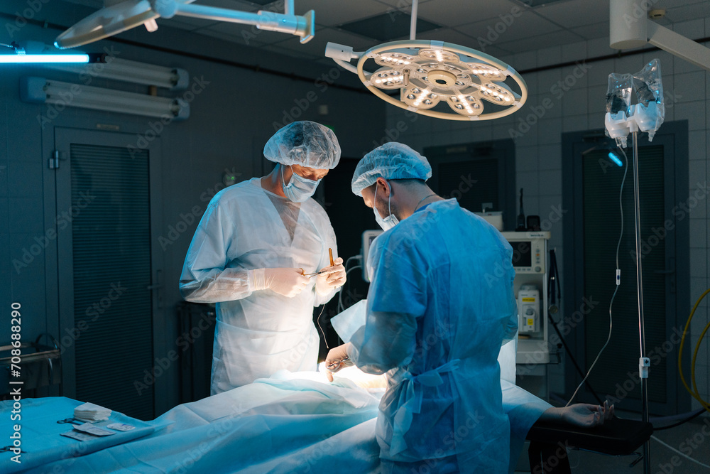 Rear view of team of professional surgeons performing invasive surgery ...