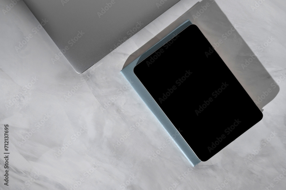 Tablet with black screen, notebook, closed laptop computer on gray ...