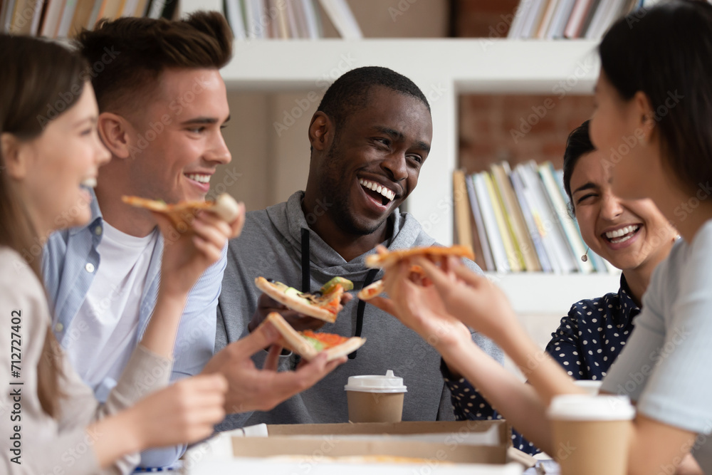 Overjoyed multiracial students friends have fun joke eating delicious ...