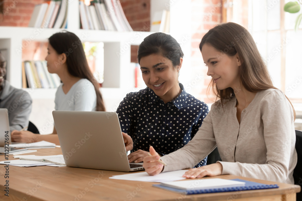 Concentrated multiracial girls sit at desk work together in groups ...
