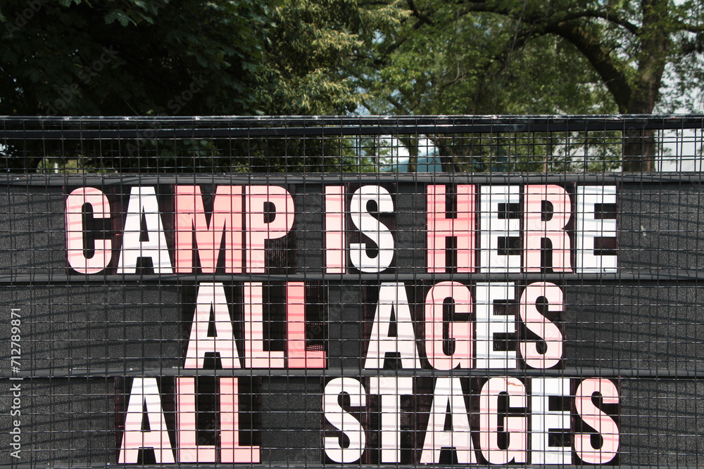 camp is here all ages all stages sign with trees in background ...
