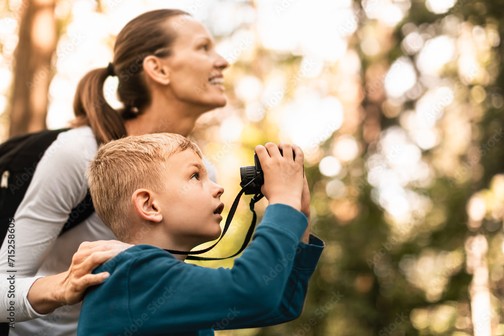 Mother child together hiking in the forest looking through binoculars ...