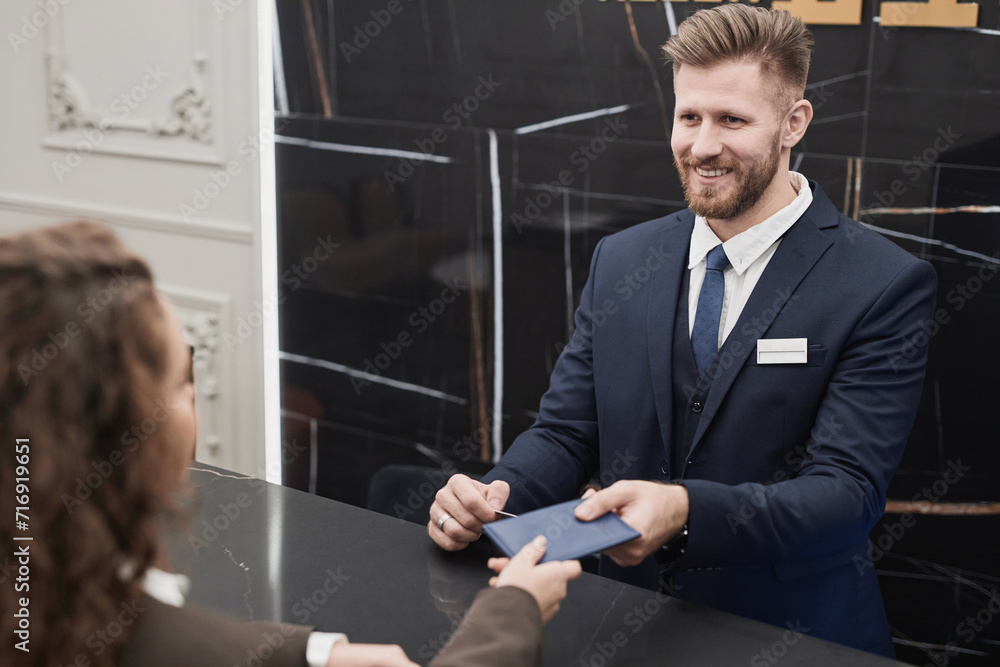 Portrait of smiling young man taking documents of hotel guest for check ...